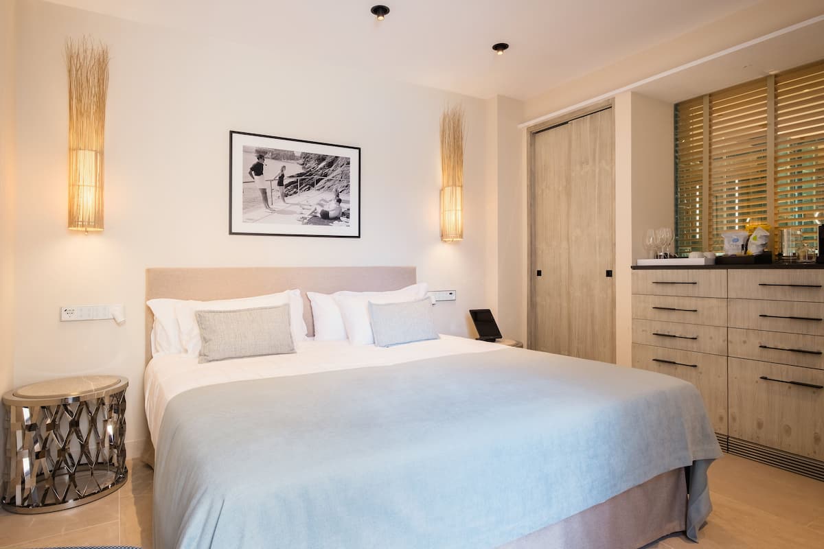 Um quarto bem organizado com uma cama grande, luminárias de cabeceira, mesa de cabeceira, guarda-roupa e um quadro na parede.