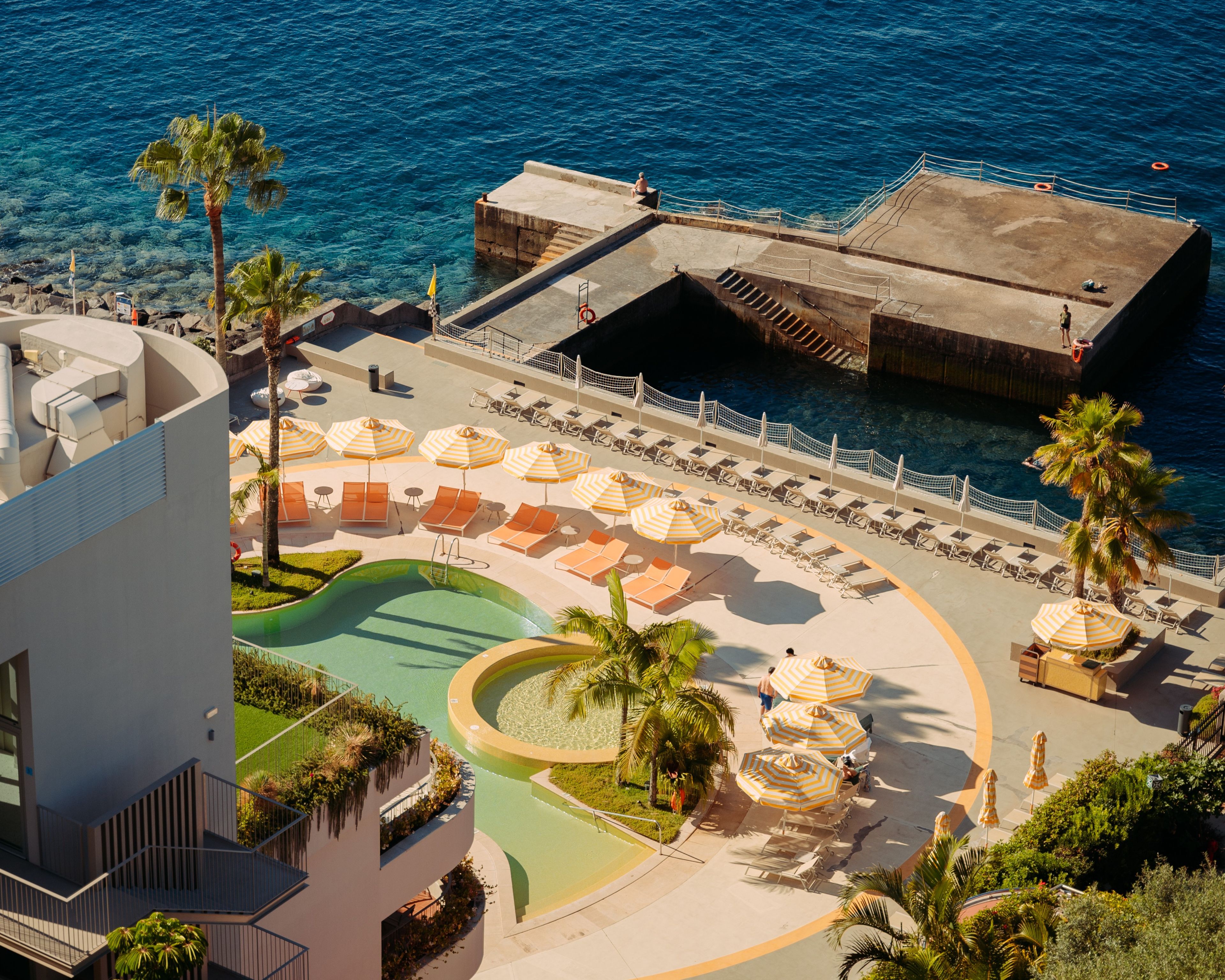 Um resort com área de piscina, espreguiçadeiras e vista para o mar.