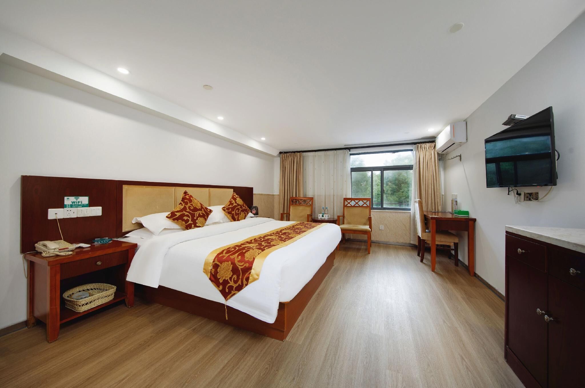 Quarto de hotel com uma cama grande, uma escrivaninha, uma cadeira, uma televisão e uma janela com cortinas.