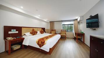 Quarto de hotel com uma cama grande, uma escrivaninha, uma cadeira, uma televisão e uma janela com cortinas.