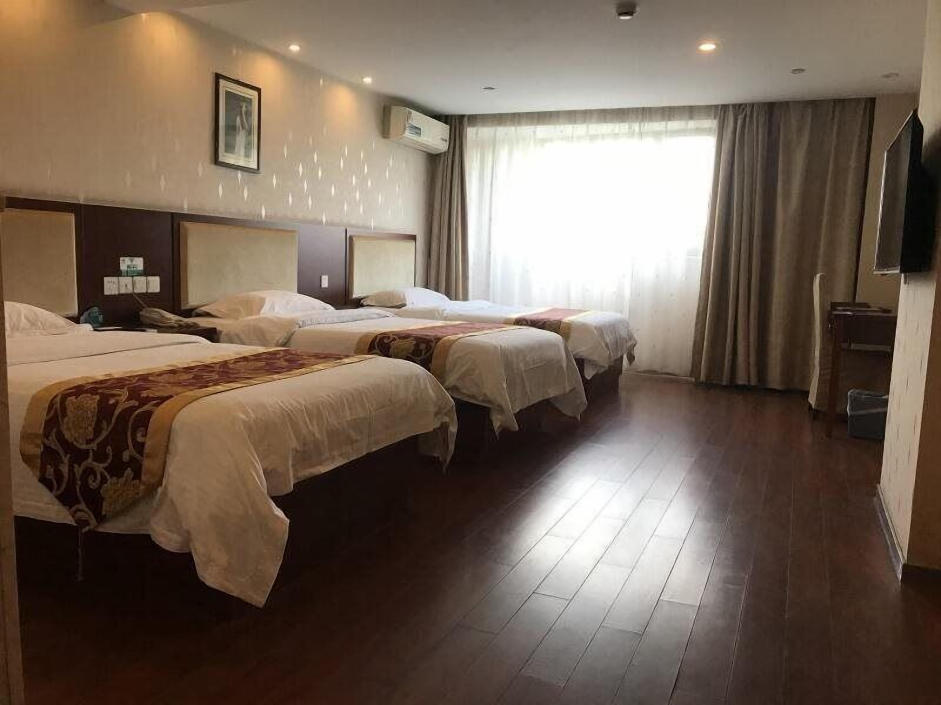 Quarto de hotel com três camas, televisão de tela plana, escrivaninha e uma grande janela com cortinas.