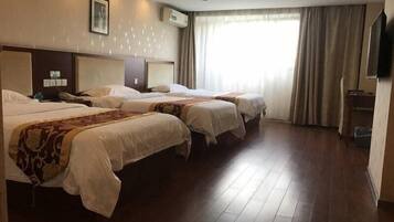 Quarto de hotel com três camas, televisão de tela plana, escrivaninha e uma grande janela com cortinas.