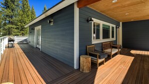 Um deck de madeira com área de estar integrada e uma pequena mesa, rodeado por um edifício azul escuro com detalhes brancos.