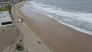 Uma praia com um calçadão pavimentado, bancos e uma cerca ao longo da orla.