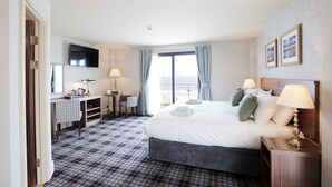 Quarto de hotel com uma cama grande, uma escrivaninha com cadeira, televisão e janela com cortinas.