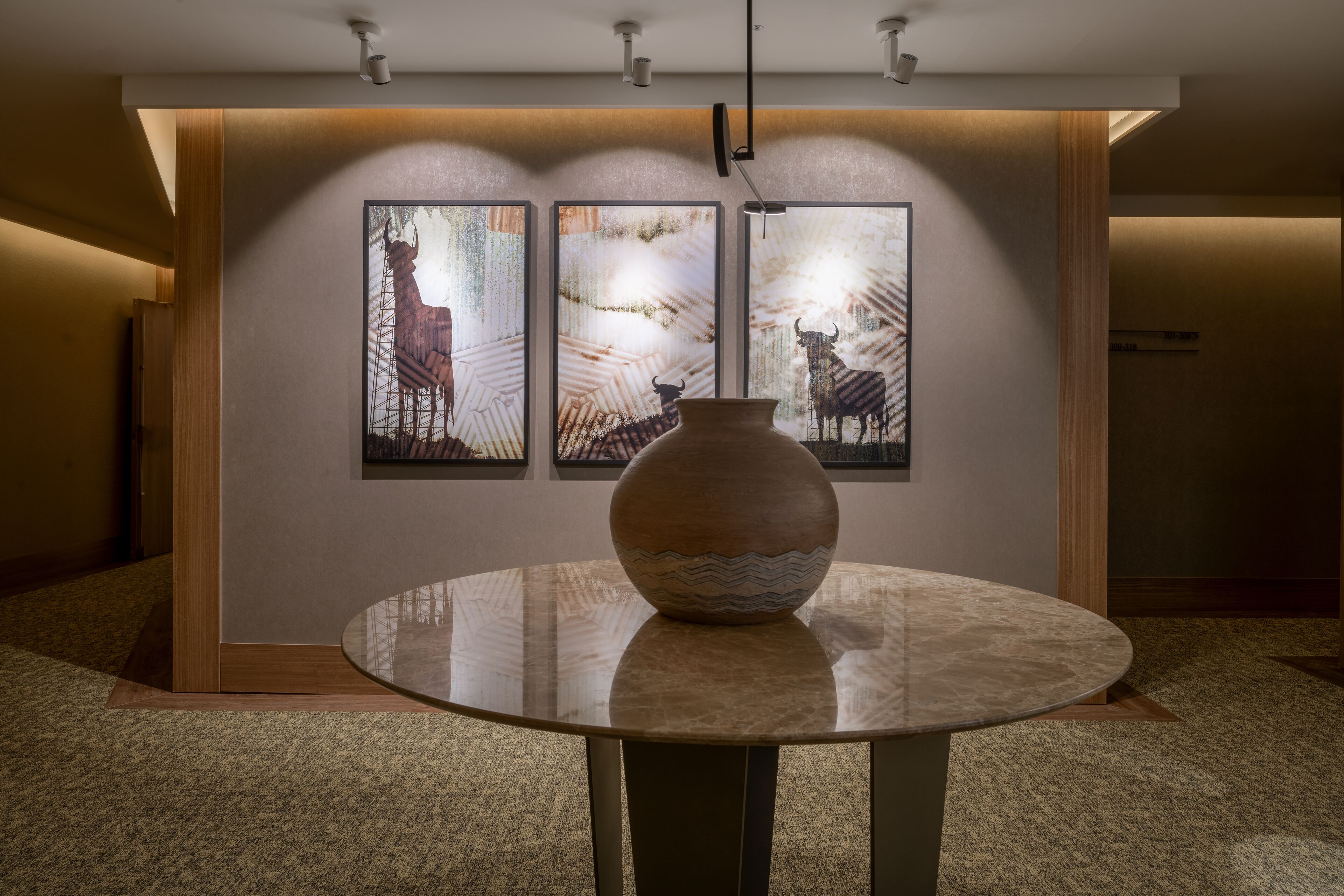 Um interior moderno com uma mesa redonda, um vaso grande e três obras de arte emolduradas na parede.