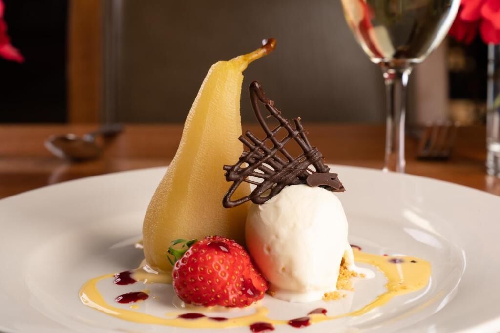 Um prato de sobremesa com uma pêra, treliça de chocolate e uma morango.
