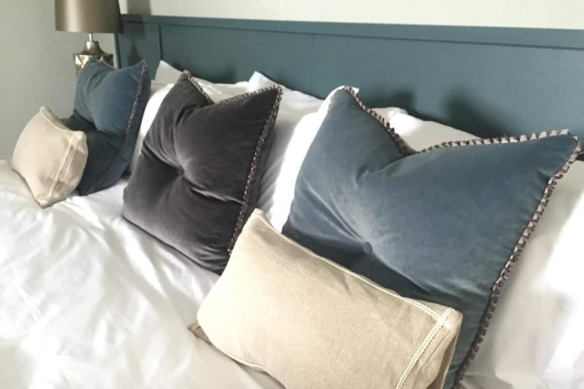 Cama bem arrumada com várias almofadas em cores e texturas diferentes.