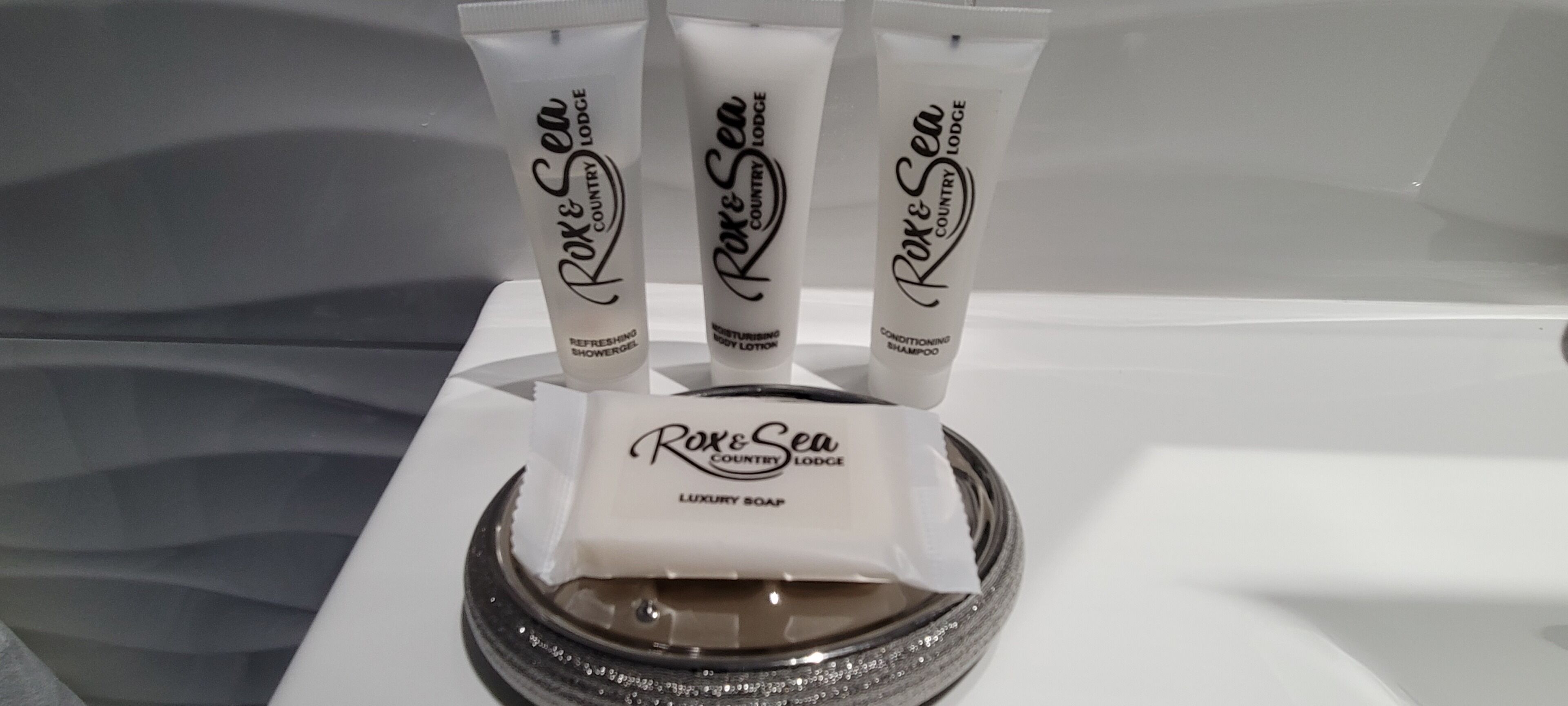 Uma pia de banheiro com três frascos de shampoo Roxy & Sea Country Lodge e um sabonete artesanal de luxo Roxy & Sea Country Lodge.