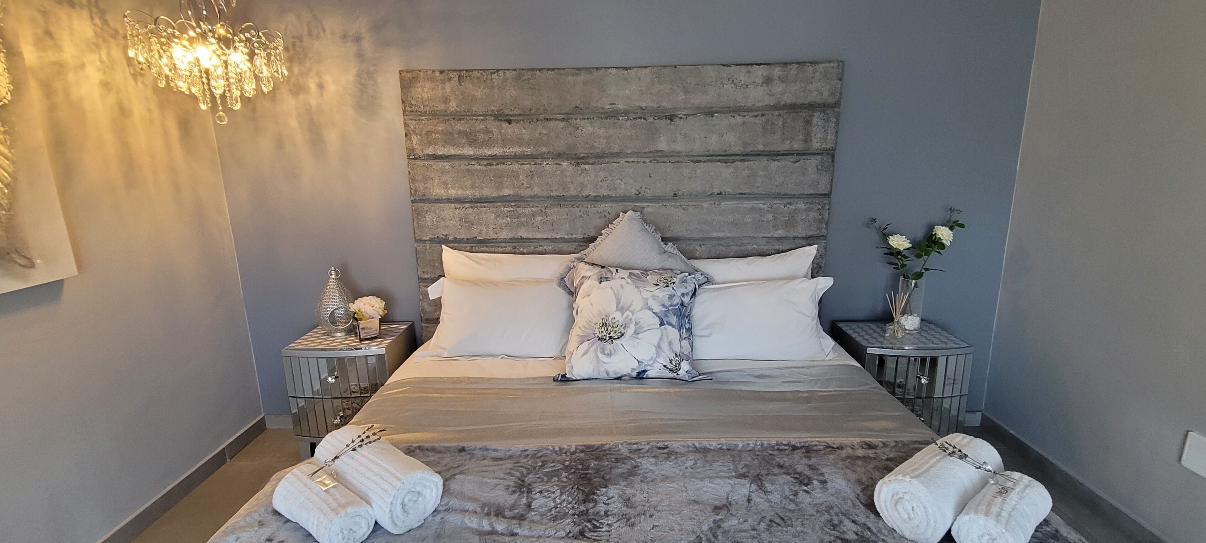Quarto com uma cama grande, duas mesas de cabeceira, um lustre e uma obra de arte na parede.