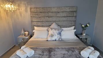 Quarto com uma cama grande, duas mesas de cabeceira, um lustre e uma obra de arte na parede.