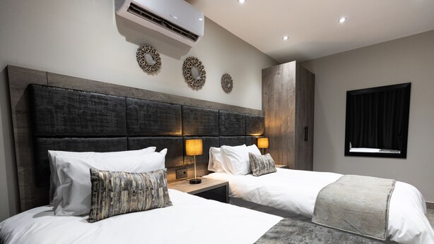 Quarto de hotel com duas camas, cabeceira moderna, decoração na parede e janela com cortinas.