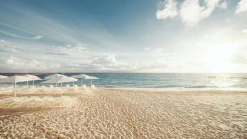 Uma praia com guarda-sóis brancos e espreguiçadeiras.