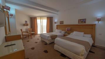 Quarto de hotel com duas camas, uma escrivaninha, uma cadeira e uma janela grande com cortinas.
