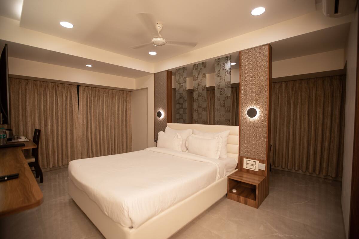 Quarto de hotel moderno com uma cama grande, uma mesa de cabeceira de madeira, uma escrivaninha e um ventilador de teto.