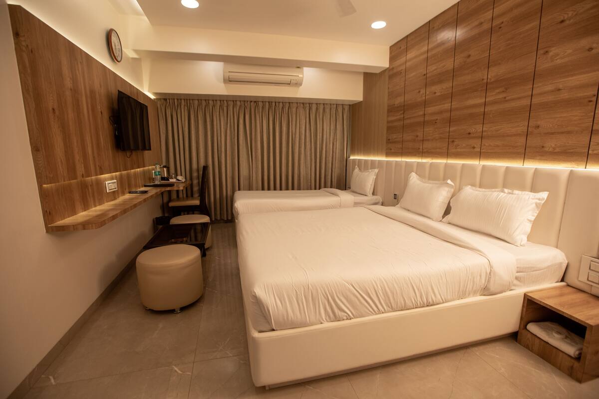 Quarto de hotel moderno com uma cama grande, uma escrivaninha, uma cadeira e uma TV fixada na parede.