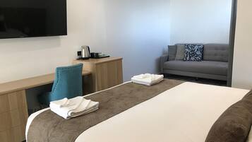 Quarto de hotel com cama, escrivaninha, cadeira, sofá e televisão de tela plana.