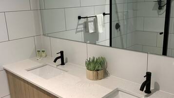 Uma casa de banho moderna com toucador de madeira, duas pias, um espelho e zona de duche.