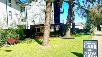 Um café com mesas ao ar livre, um letreiro indicando que está aberto e um prédio ao fundo.