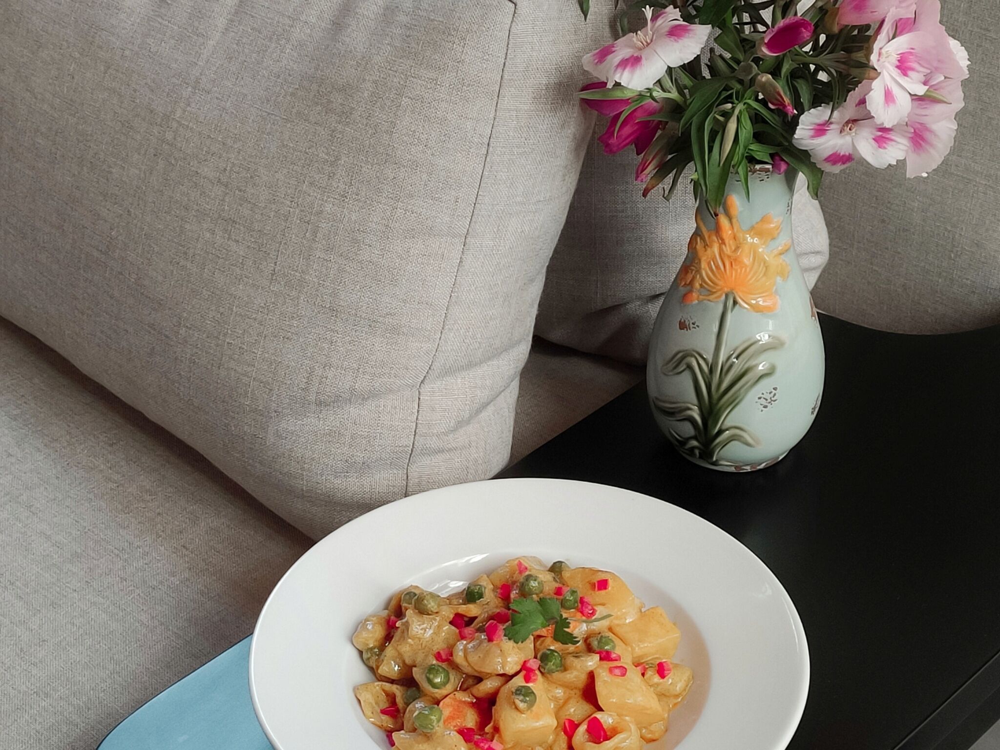 Um prato de comida sobre uma mesa, ao lado de um sofá e um vaso com flores.
