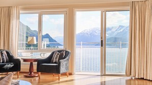 Quarto com grande porta de correr de vidro que dá para uma varanda com vista para a montanha. Há duas poltronas e uma pequena mesa com abajur.