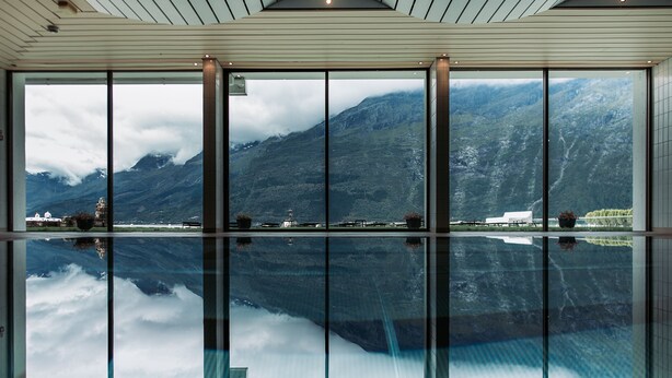 Piscina interior moderna com vista clara para uma paisagem montanhosa através de amplas janelas.
