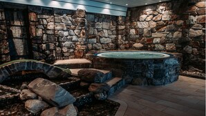 Área de spa com paredes de pedra, banheira de hidromassagem e uma pequena cascata.