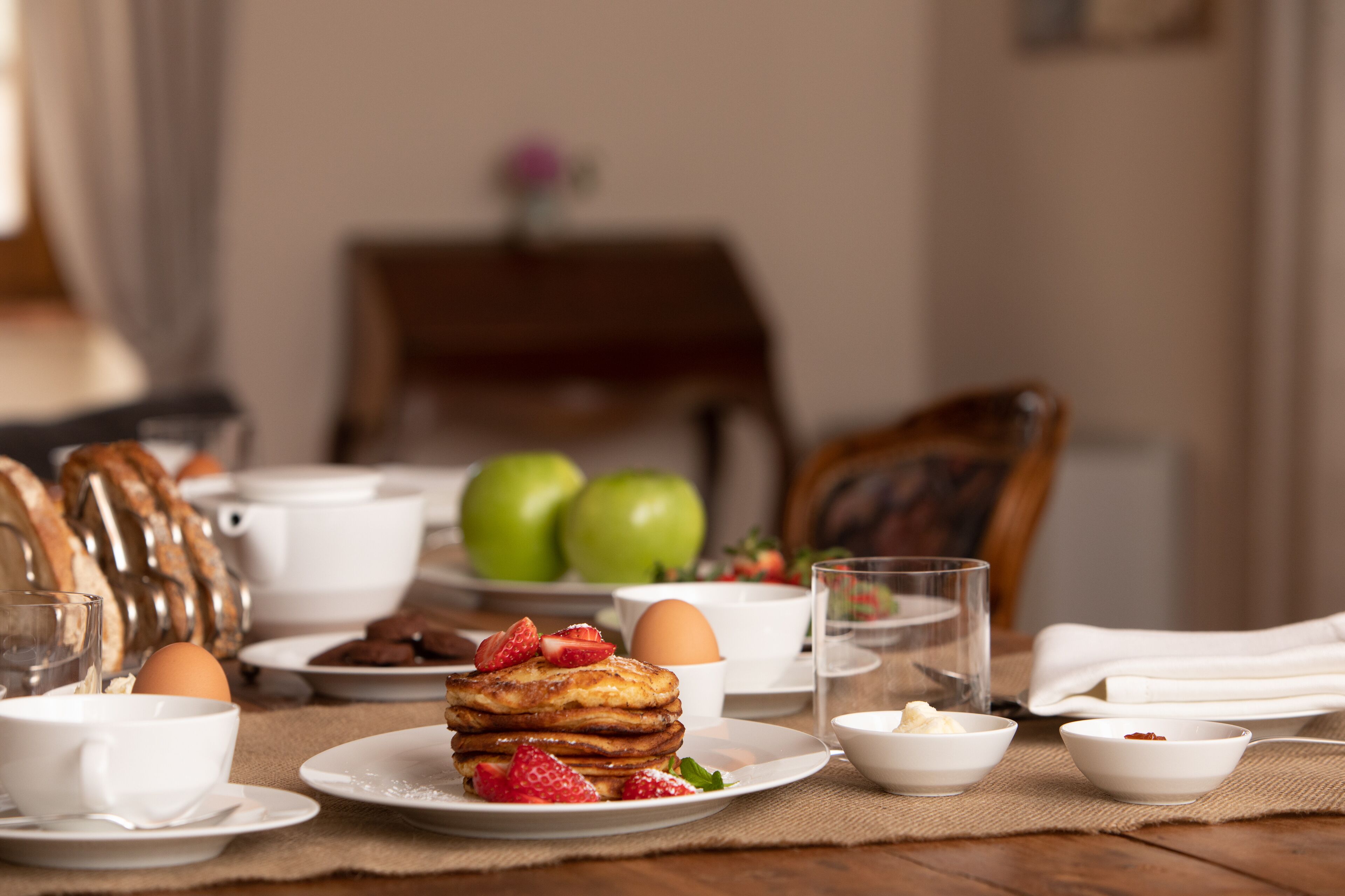 Uma mesa de café da manhã com panquecas, morangos, ovos e maçãs.