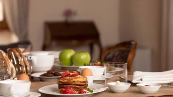 Uma mesa de café da manhã com panquecas, morangos, ovos e maçãs.