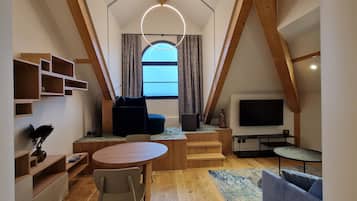 Um espaço compacto com cama beliche, mesa de jantar redonda, TV fixada na parede e uma janela grande com cortinas.