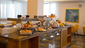 Buffet com diversos alimentos, uma máquina de café e um quadro na parede.