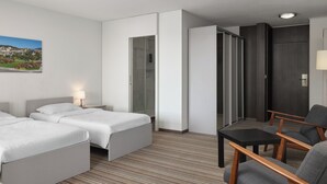 Quarto de hotel com duas camas, uma escrivaninha, uma cadeira, chuveiro e vista para a cidade.