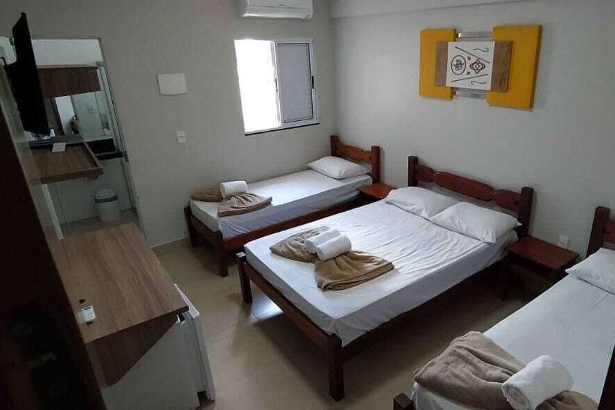 Quarto com duas camas de solteiro, uma escrivaninha de madeira, um espelho e uma pequena janela.