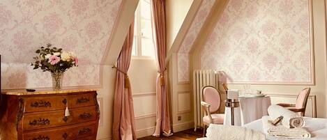 Quarto com cômoda de madeira, penteadeira com espelho, cama com roupa de cama branca e janela com cortinas.