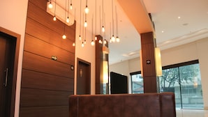 Um hall moderno com balcão de recepção, painéis de madeira, luminárias pendentes e entrada de vidro.