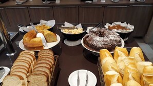 Buffet com diversos pães e produtos de pastelaria, incluindo uma placa com 'Pão de Sal Integral'.