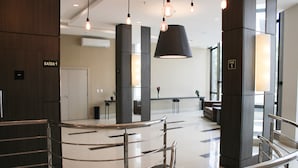 Um lobby moderno com área de estar central, escada e placa indicando a saída.