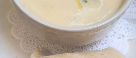 Uma tigela de sopa cremosa com um enfeite, acompanhada de uma tortilla enrolada num prato.