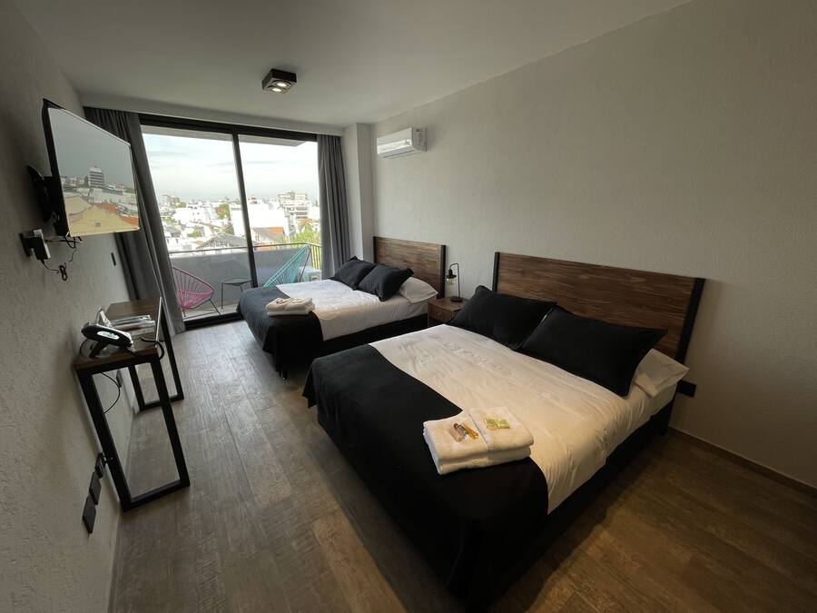 Quarto de hotel com duas camas, televisão, escrivaninha e varanda com vista para a cidade.