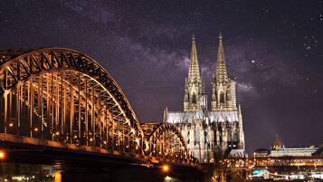 Vista noturna de uma grande ponte iluminada, com uma catedral ao fundo.