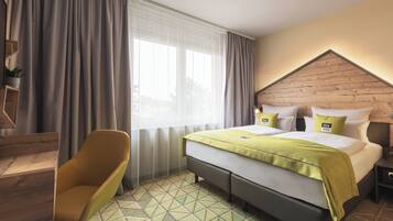 Quarto de hotel com cama, uma cadeira, mesa de cabeceira e janela com cortinas.