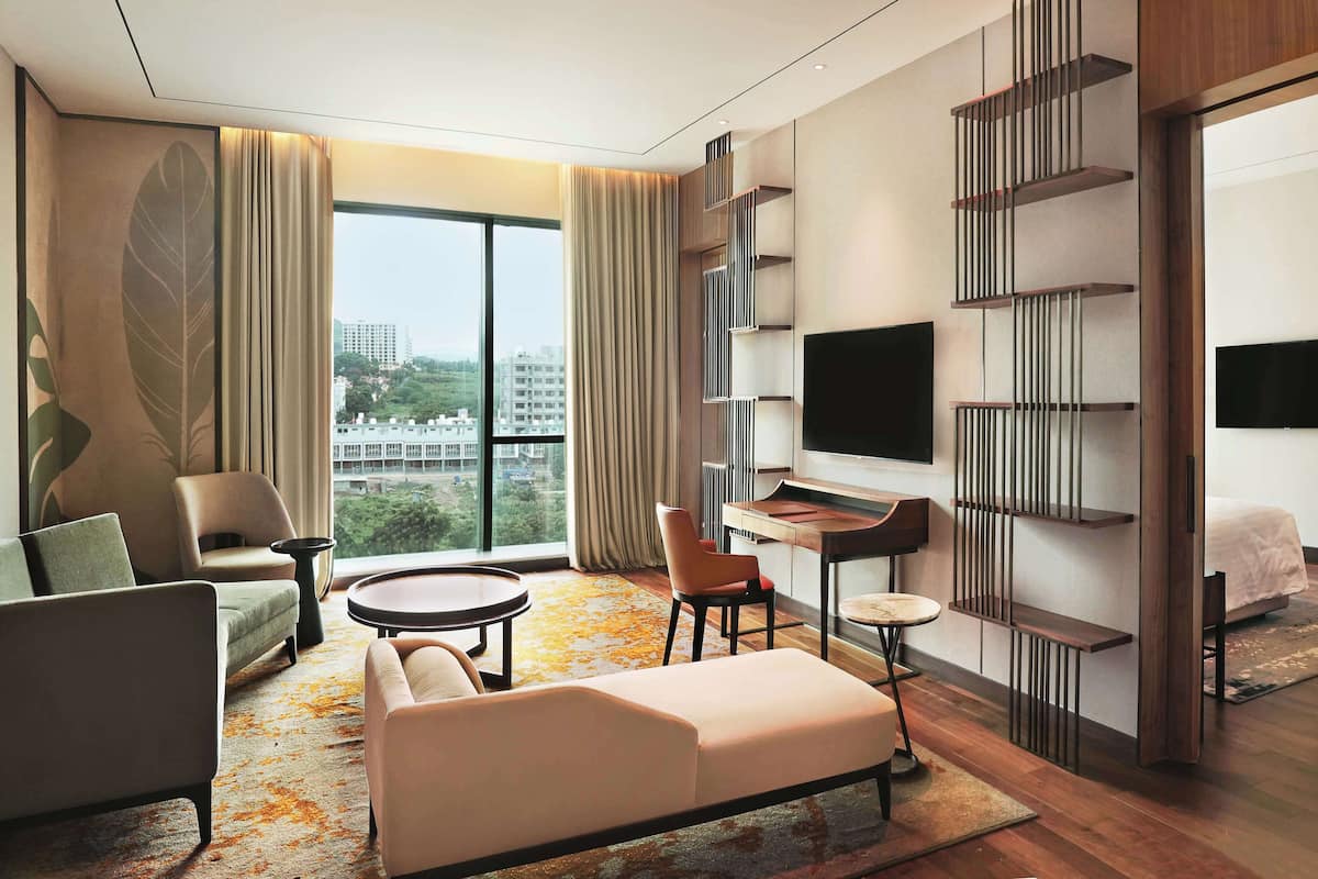 Quarto de hotel moderno com uma janela grande, um sofá, uma escrivaninha, uma cadeira e uma televisão.