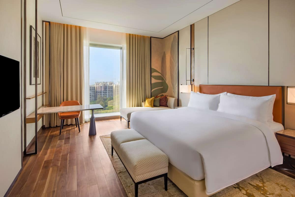 Quarto de hotel moderno com uma cama grande, uma escrivaninha e vista para a cidade.