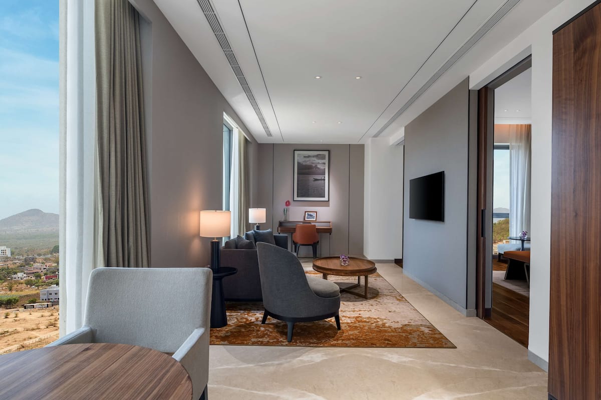 Quarto de hotel moderno com uma janela grande, um sofá, uma mesa de centro e uma televisão.