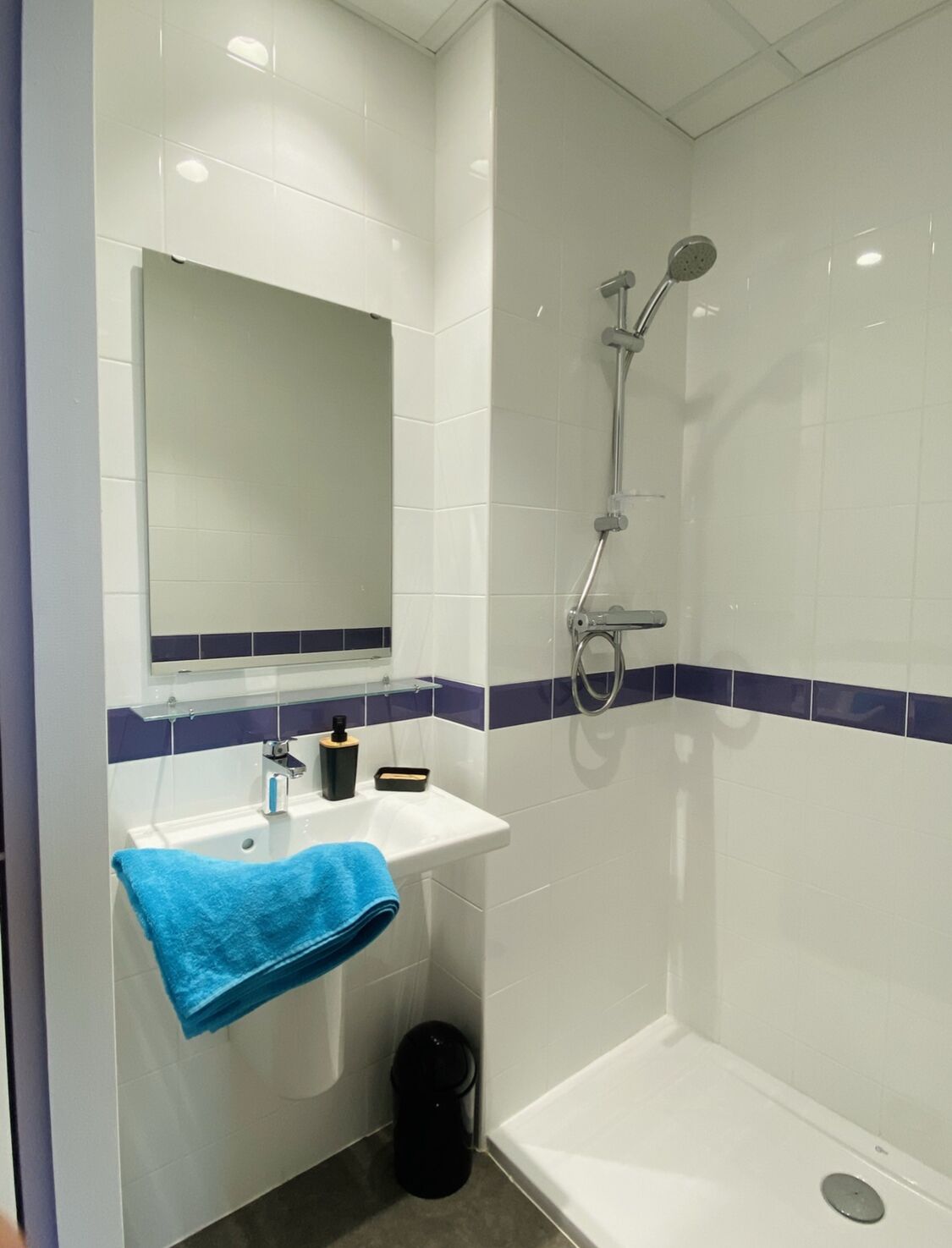 Casa de banho moderna com lavatório branco, toalha azul e chuveiro com chuveiro manual.