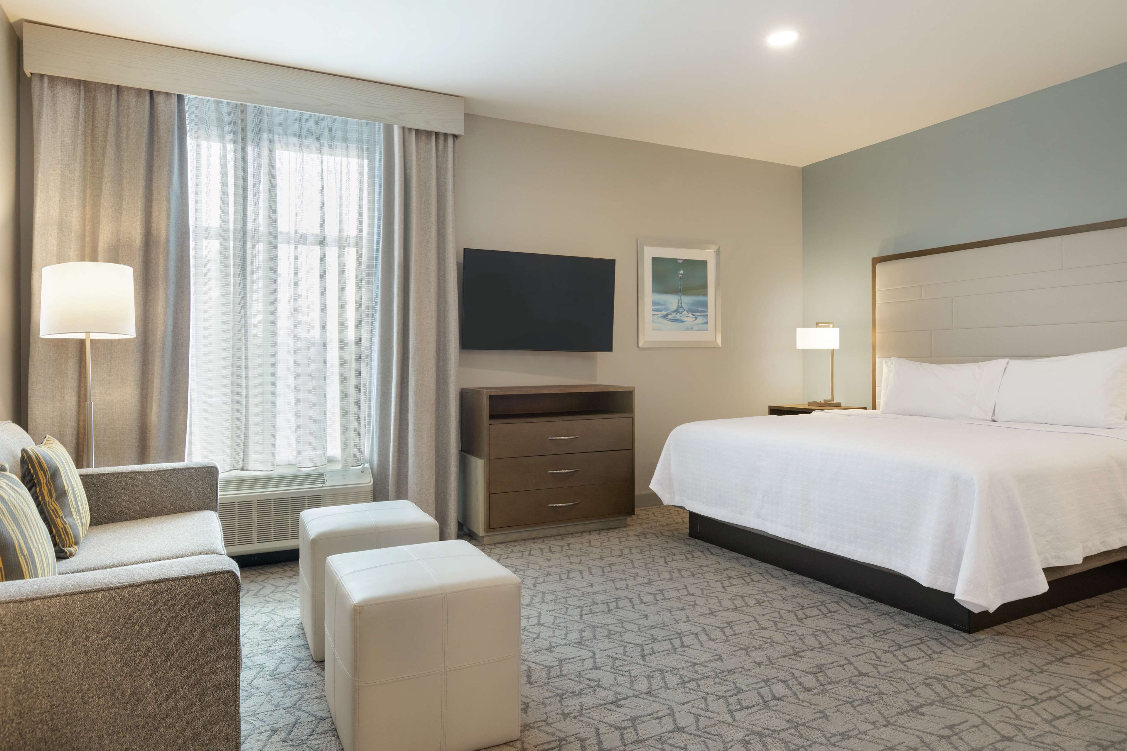 Quarto de hotel com cama, sofá, televisão, escrivaninha e janela com cortinas.