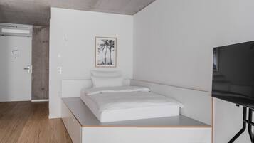 Quarto minimalista com cama, televisão e quadro na parede.
