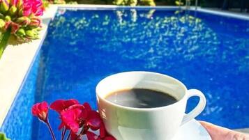 Uma chávena de café branca num pires ao lado de uma piscina com superfície de água azul cristalina.