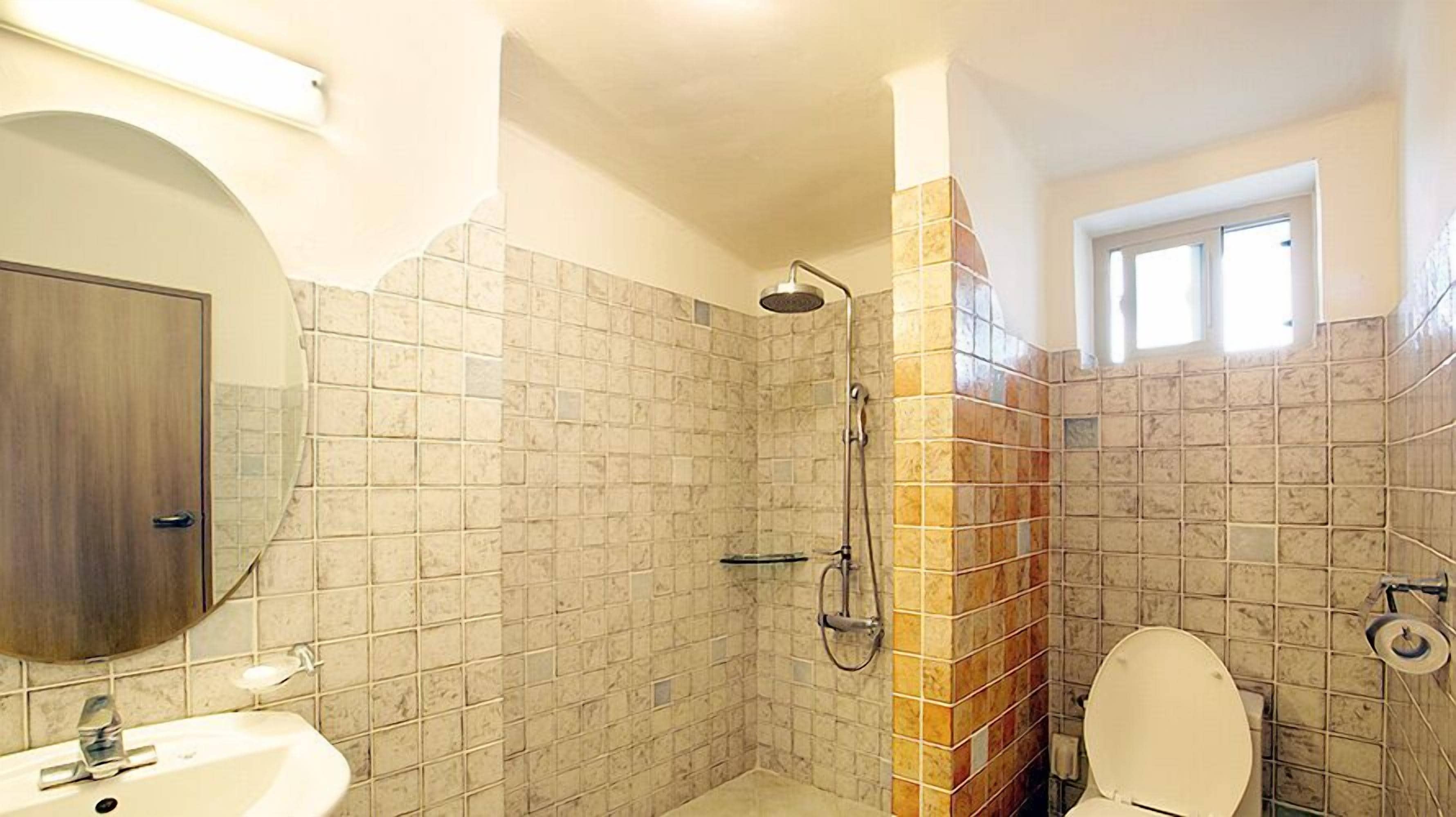 Casa de banho com chuveiro, sanita, lavatório e espelho.