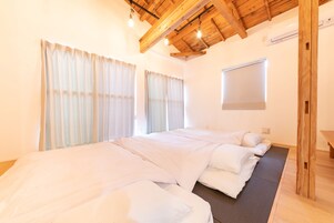 Quarto com teto de madeira, cama com roupa de cama branca e janela com cortinas.